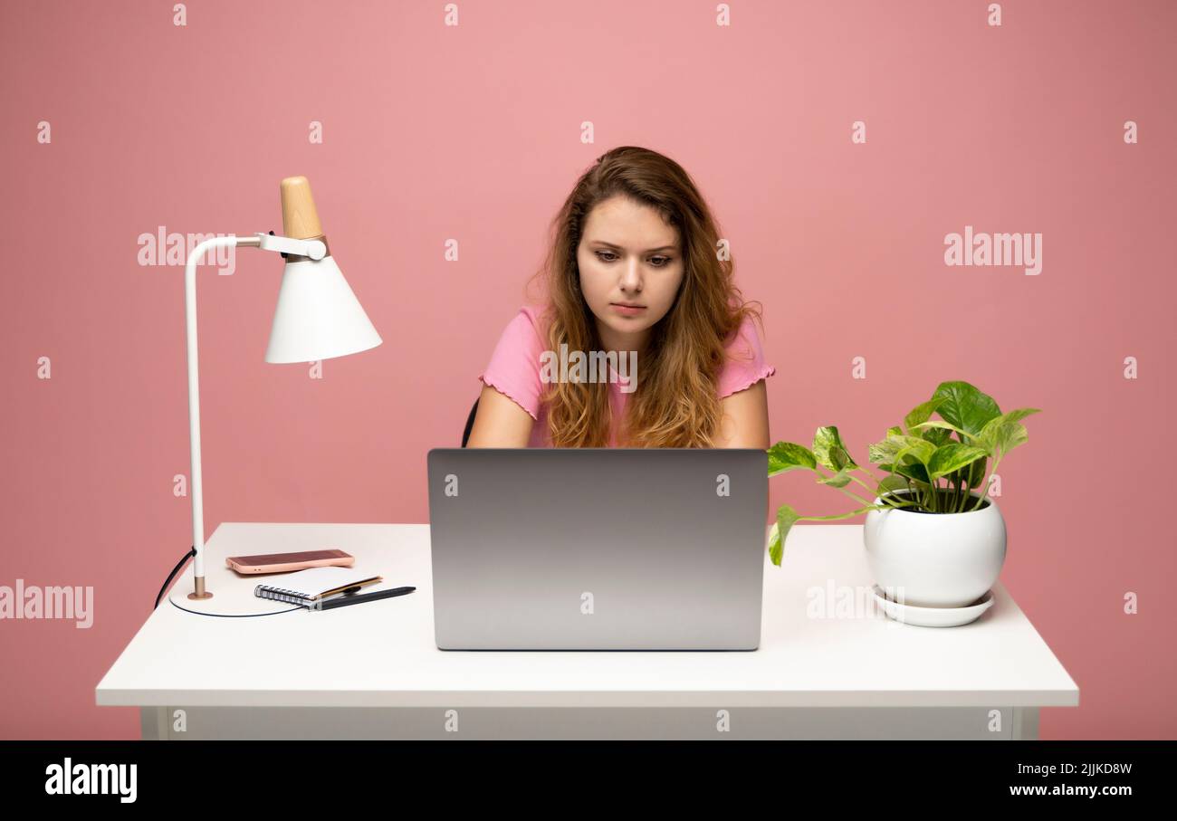 Young freelancer curly woman in a pink t-shirt working with a laptop ...