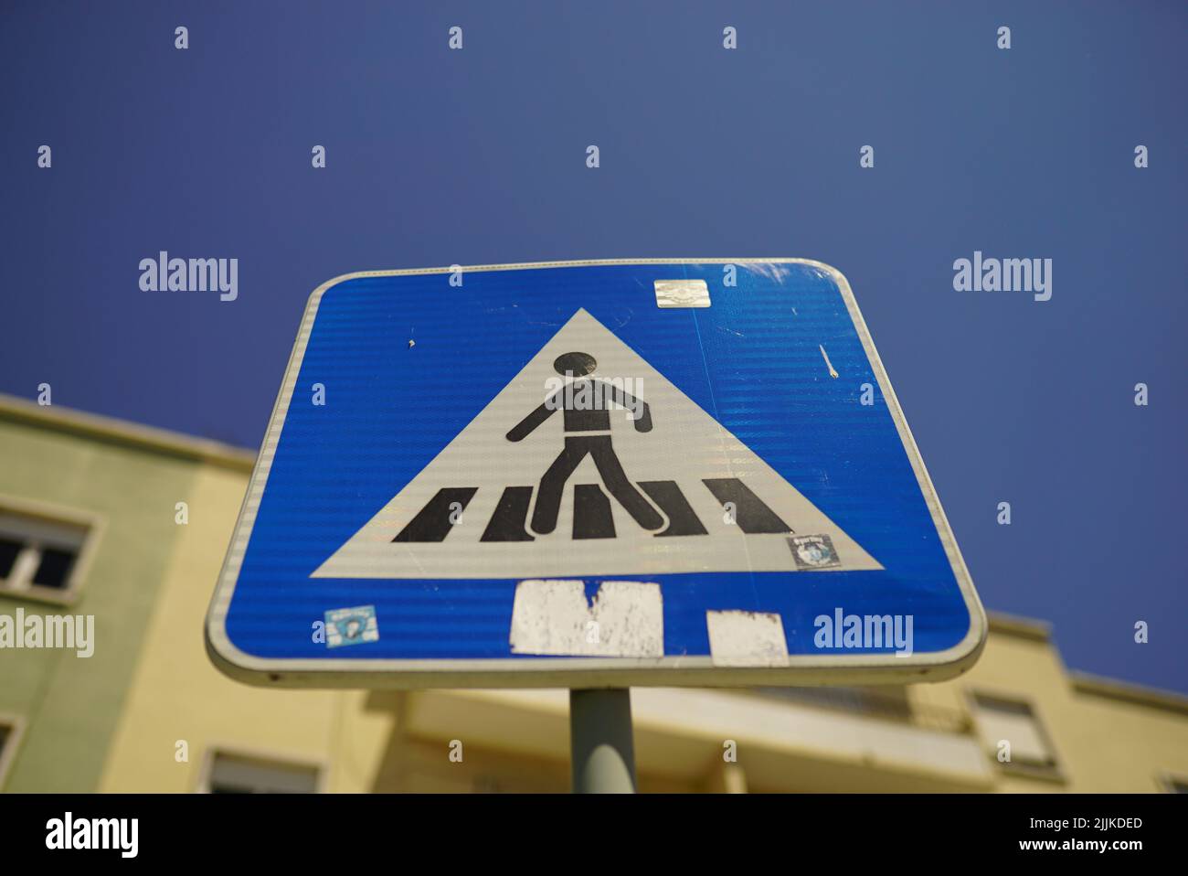 A low angle shot of a blue pedestrian crossing sign on a blue sky ...