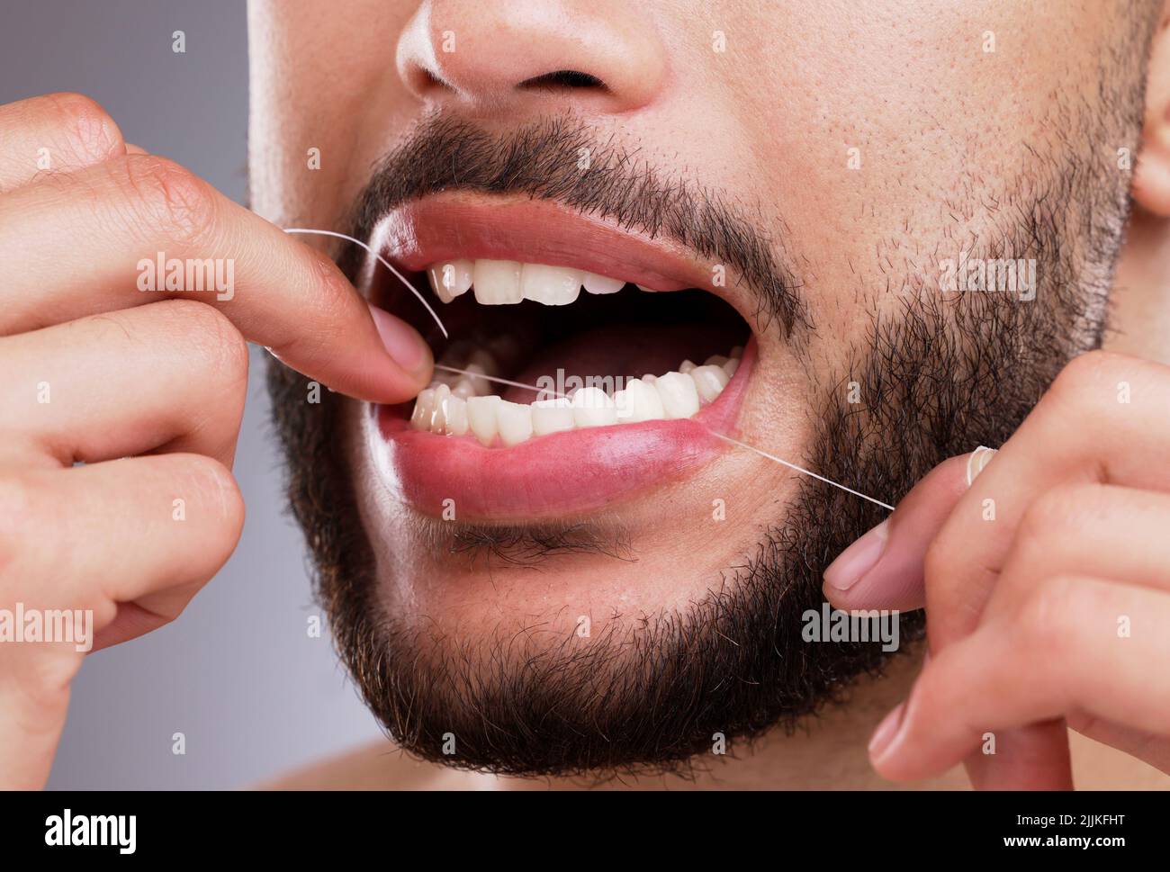 Be thorough when flossing. a man flossing his teeth against a studio background Stock Photo - Alamy