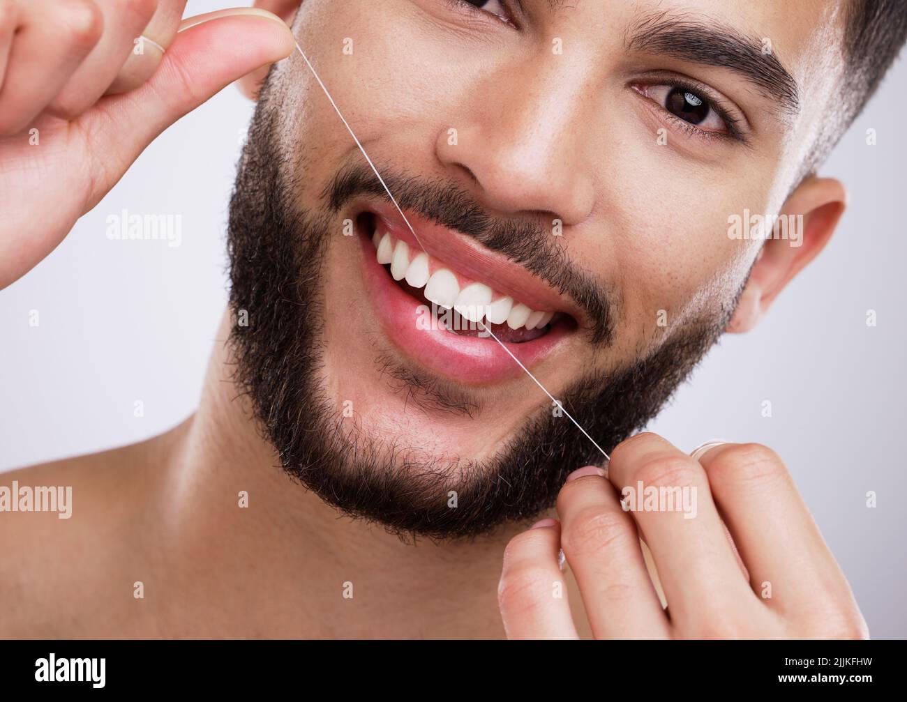 My smile is my winning feature. a young man flossing his teeth against ...