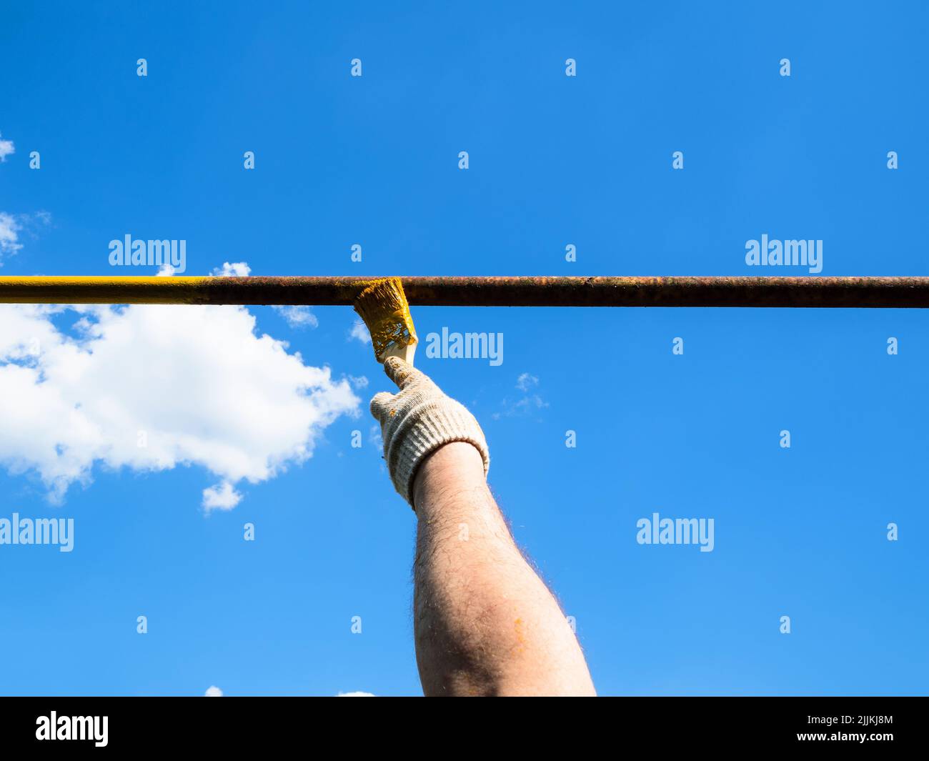 hand paints rusty outdoor gas pipe with yellow paint using brush and ...