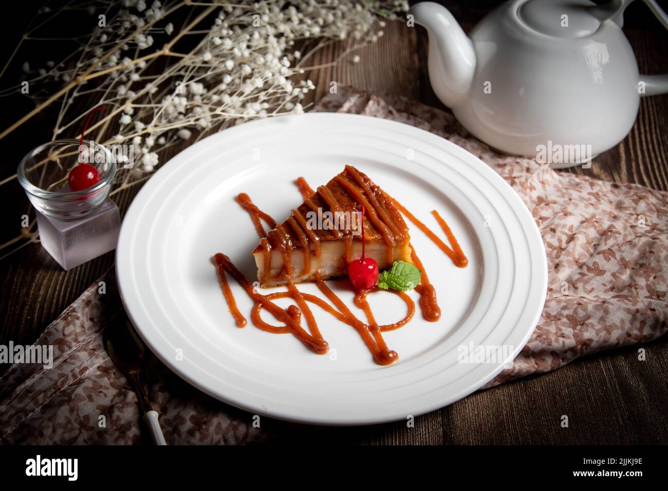An angle shot of a cake piece served with caramel topping and a cherry ...