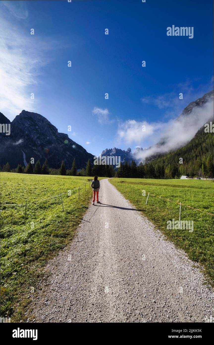 A vertical back view of a person on a trail leading to the Dolomites ...