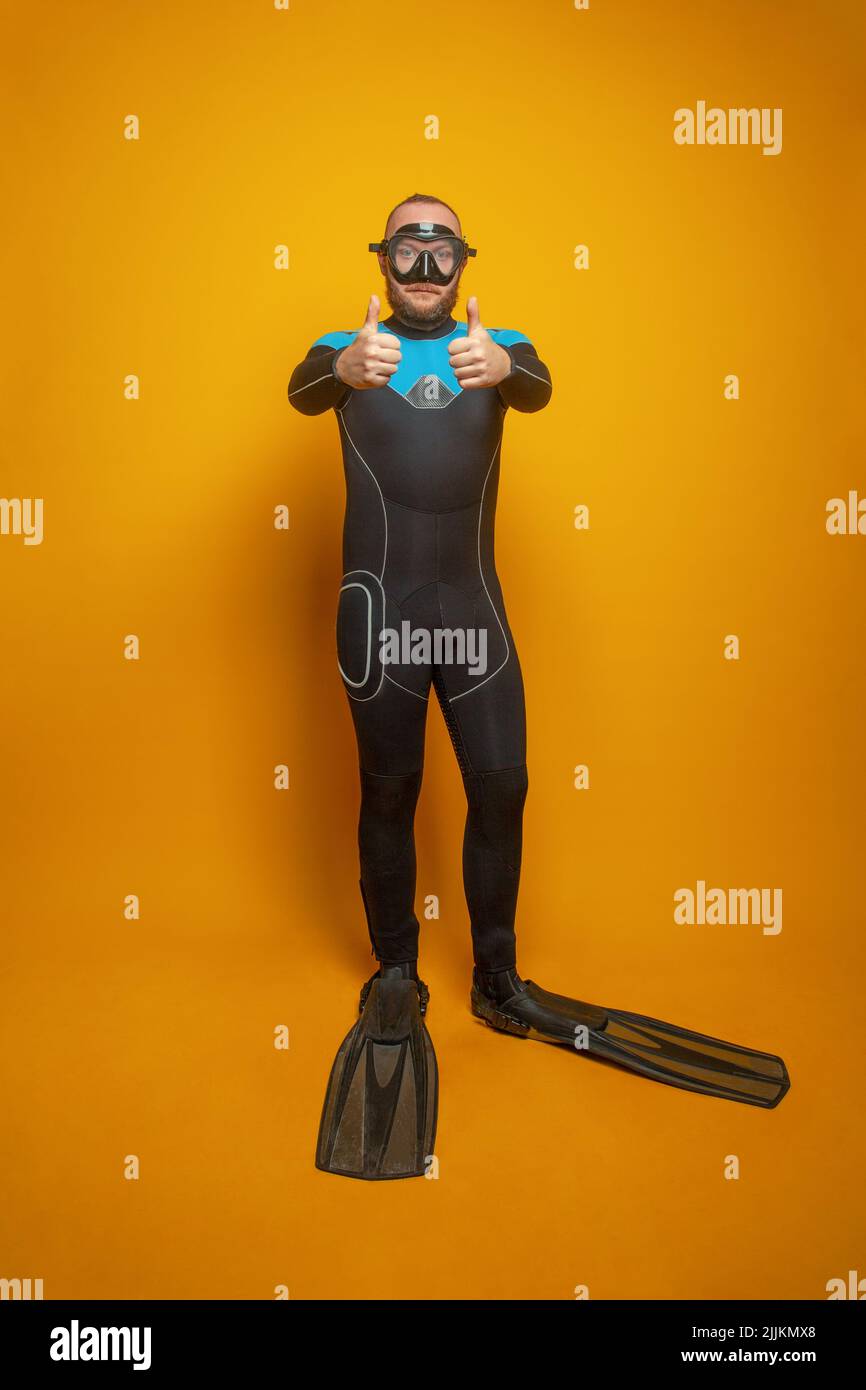 Smiling diver diving man showing thumb up against bright orange studio ...