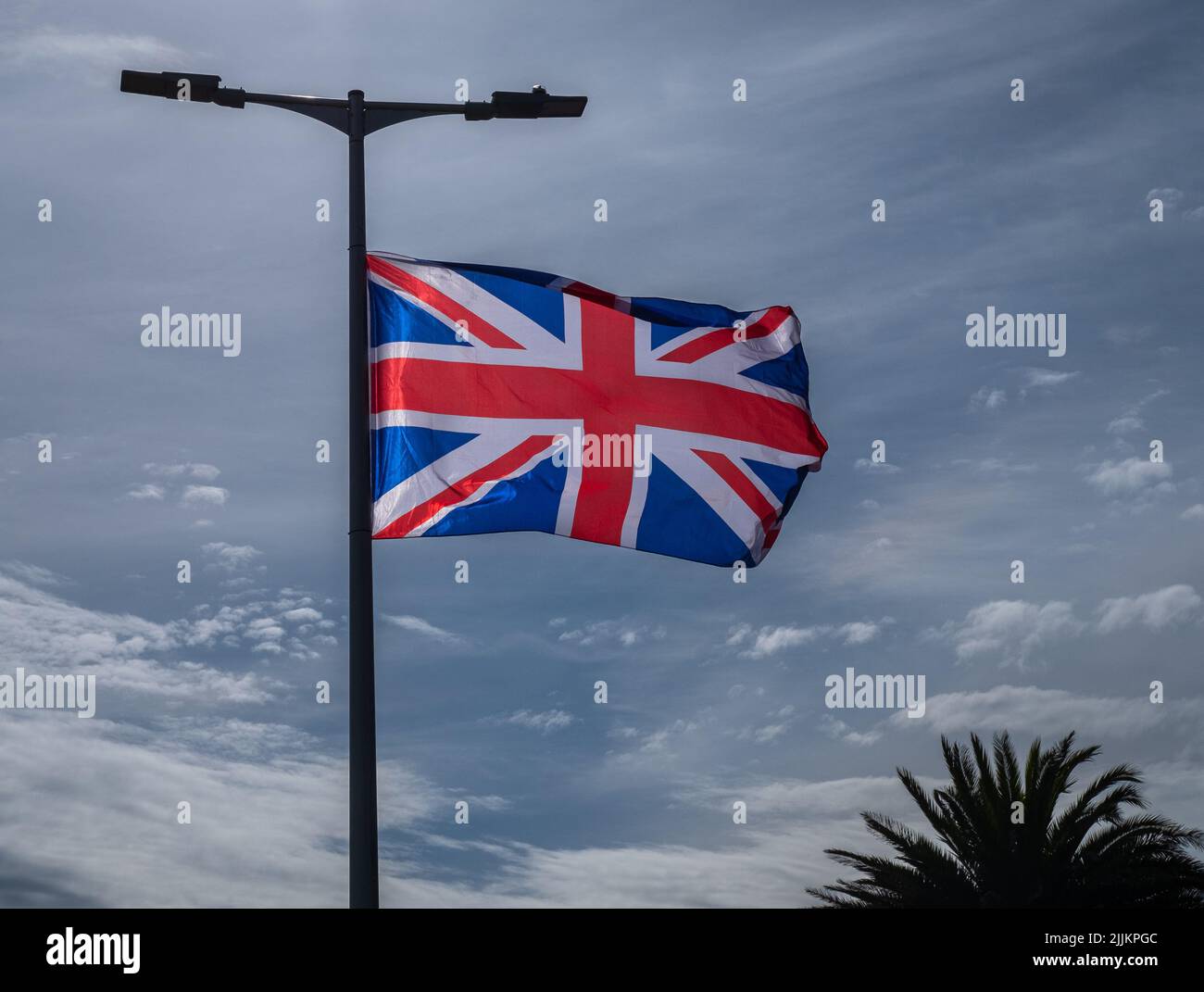 British flag on flagpole aagainst blue sky with light cloud. Flag ...