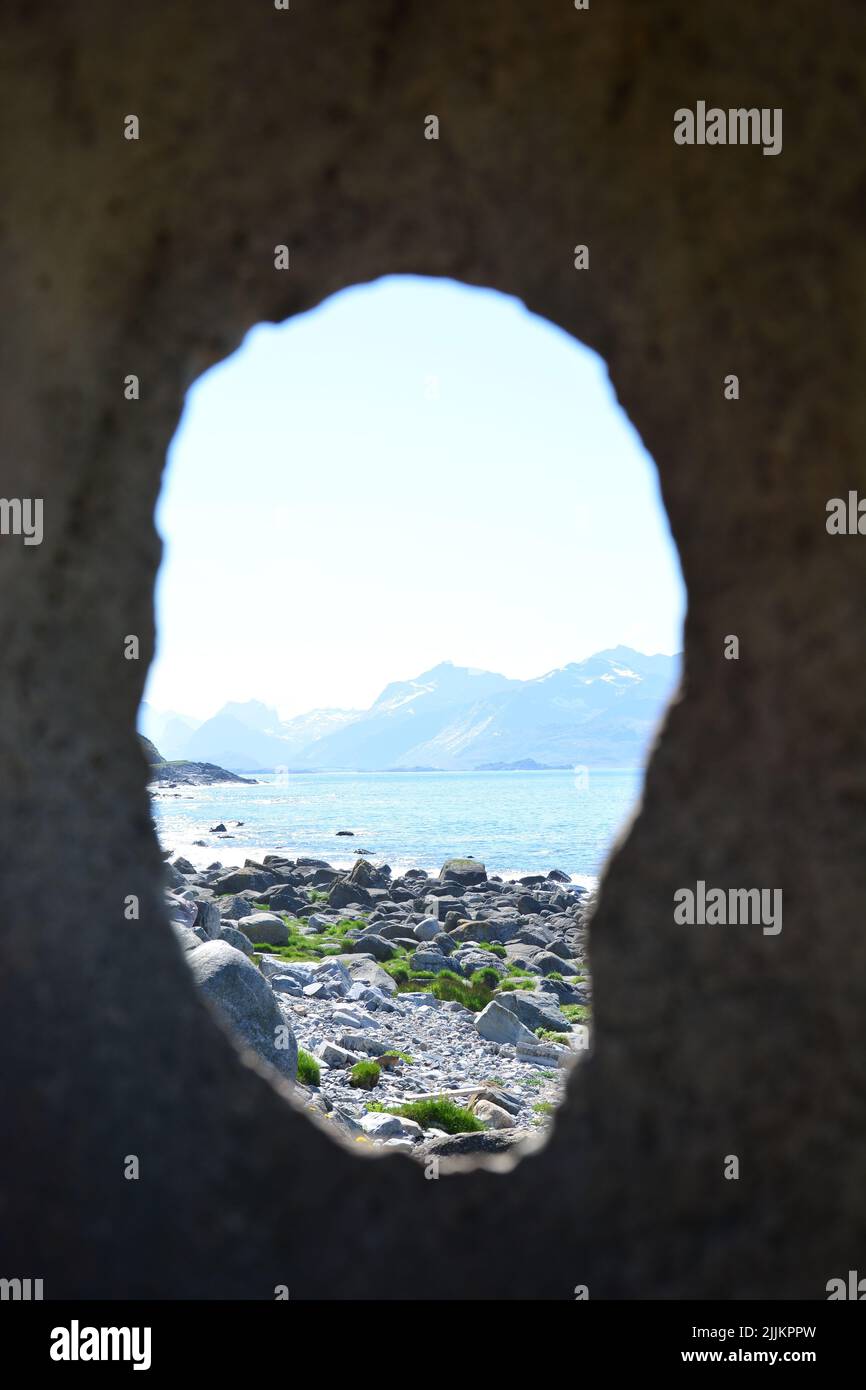 A vertical shot of a hole in a tone cave with a view of a body of water ...
