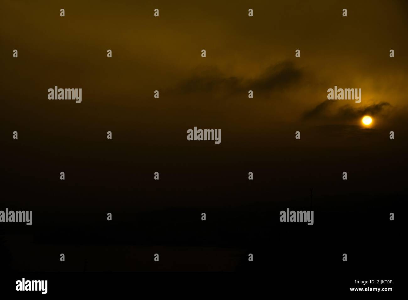 Moody sunset sky and dark clouds with a deep orange sun in stormy ...