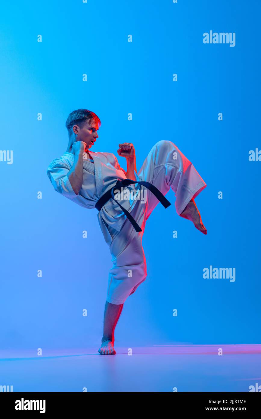 Young man, karate fighter in white kimono in action, motion isolated on ...