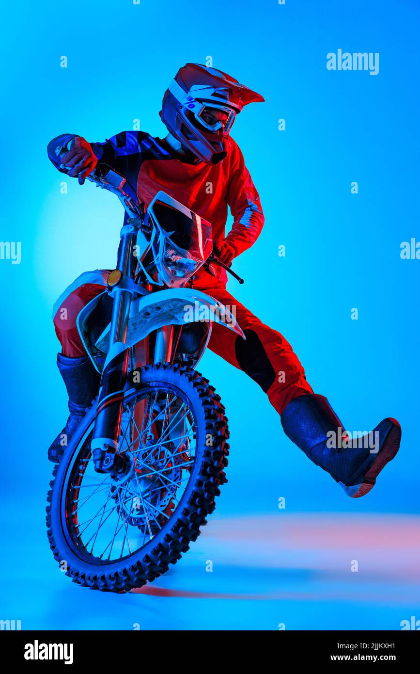 Portrait of young man, biker on motorbike isolated over blue studio ...