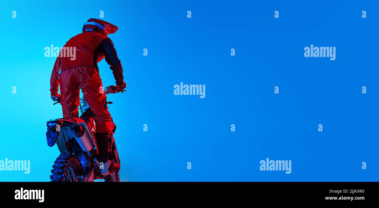 Portrait of young man, biker posing on motorbike isolated over blue ...