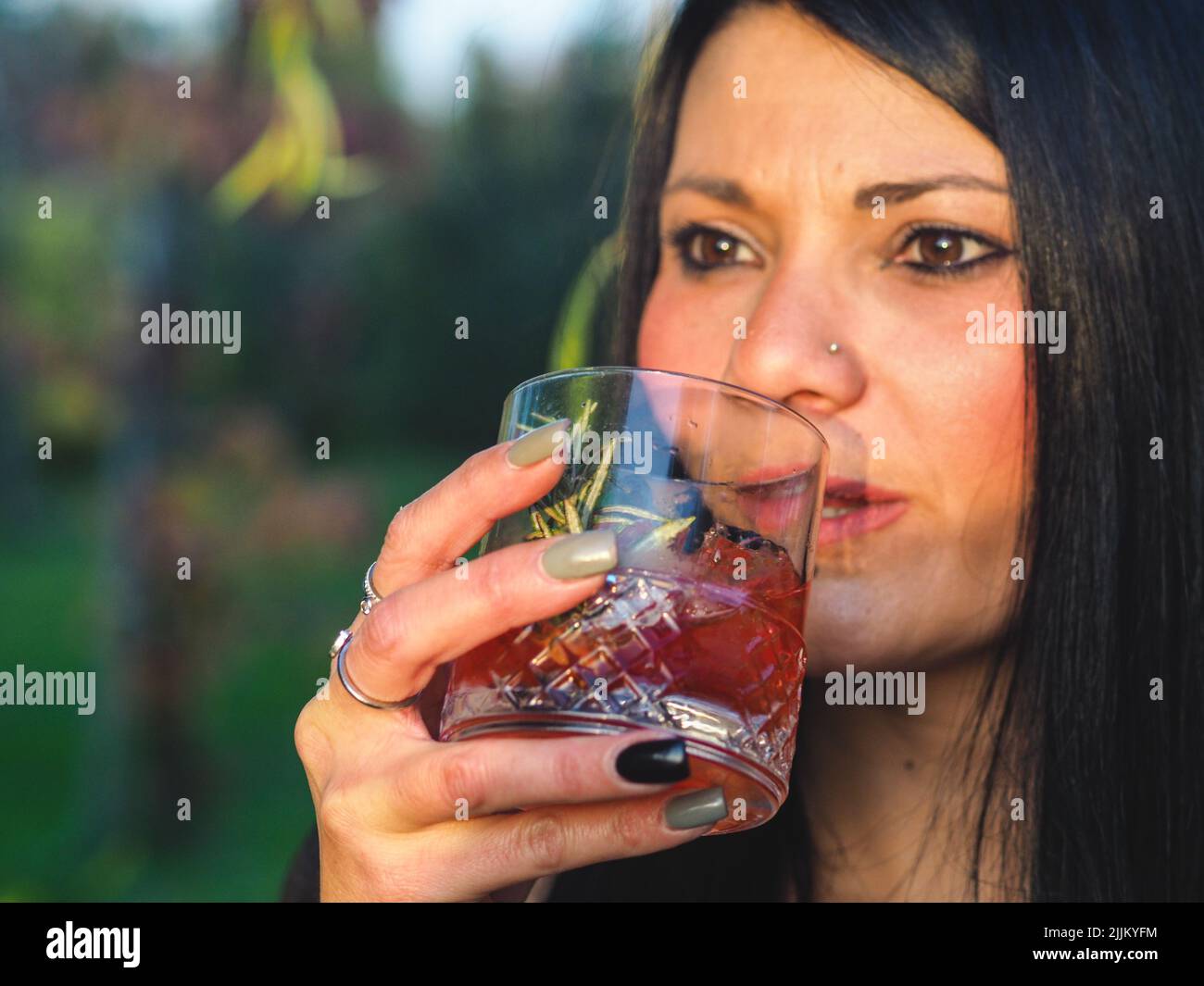 A closeup shot of a Hispanic female drinking an alcohol drink outdoors ...