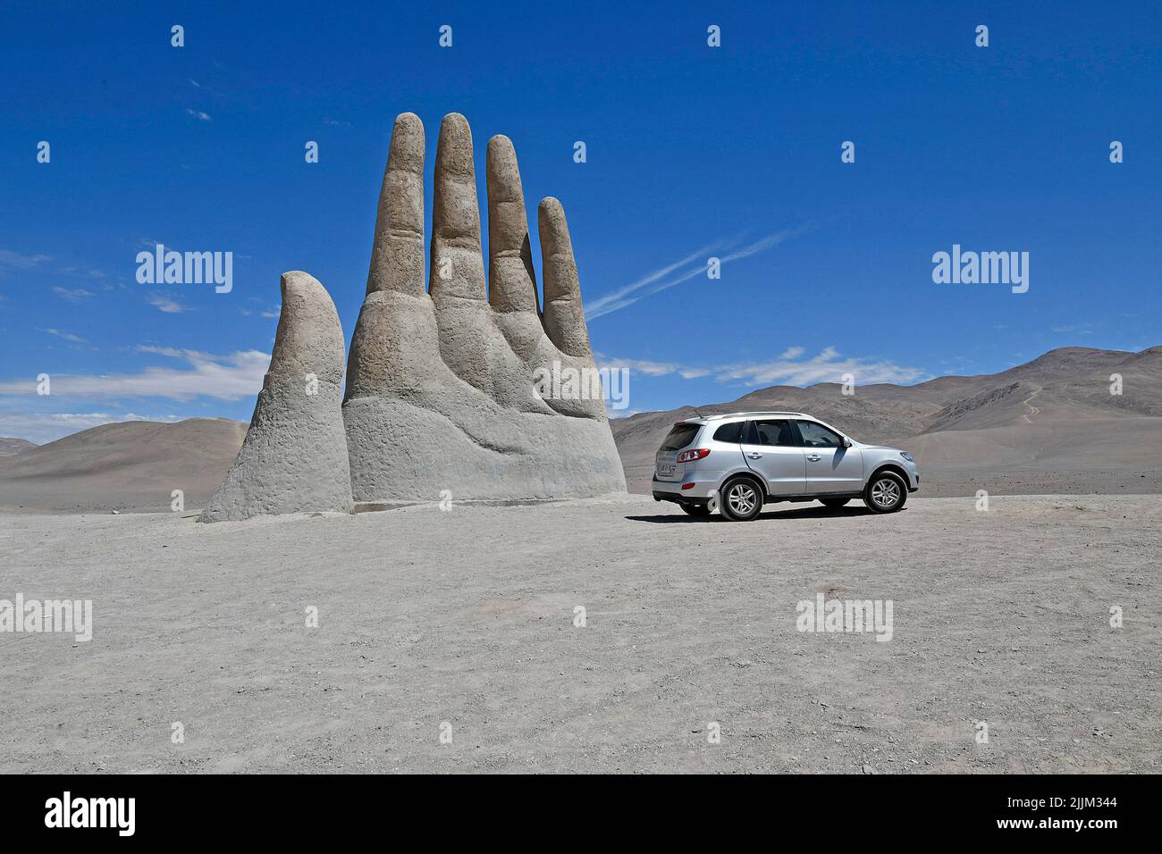 A gray car in front of a huge hand sculpture in San Pedro de Atacama ...