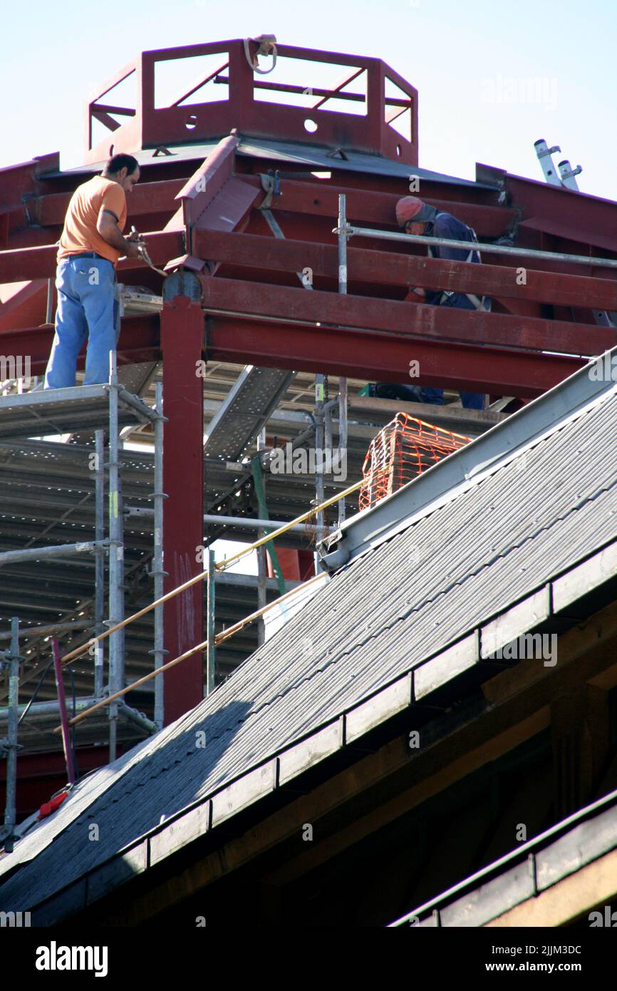 A low angle shot of two man working on a red steel structure in a ...