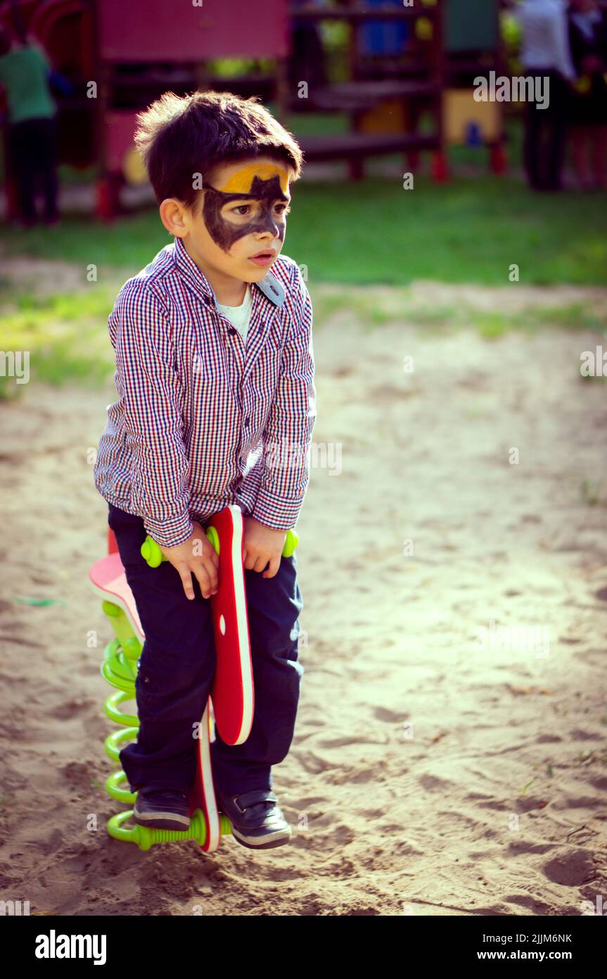 A vertical closeup of a young boy standing on a spring swing at a ...