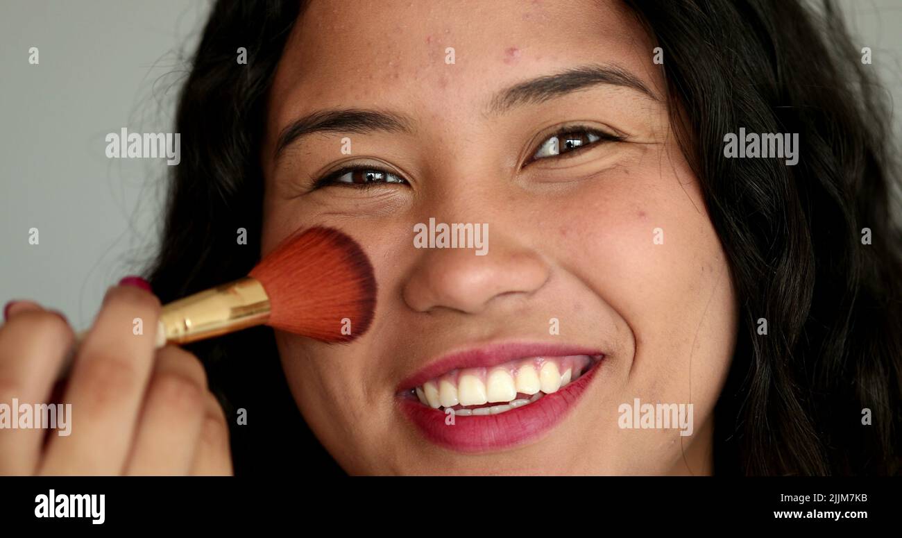 Casual Latina Hispanic woman applying make-up brush, looking at camera ...