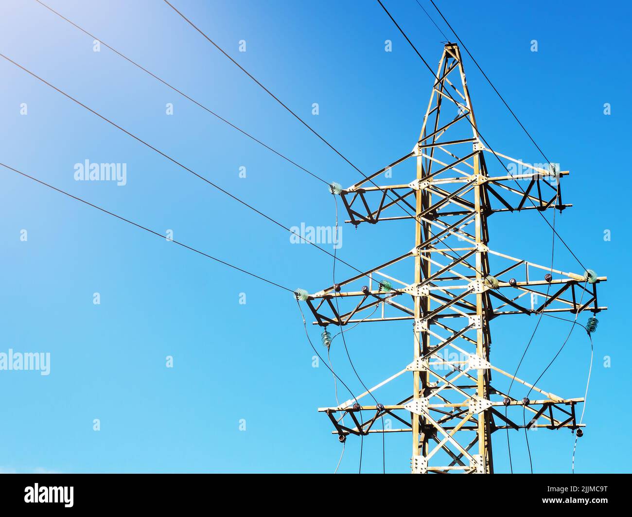 Electric pole with wires lit by the sun on a clear day under a blue sky ...