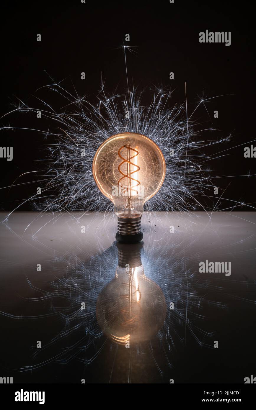 A vertical shot of an illuminated light bulb with sparks and the ...