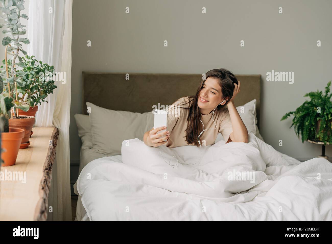 A girl in her twenties is sitting on the bed in the morning chatting on ...