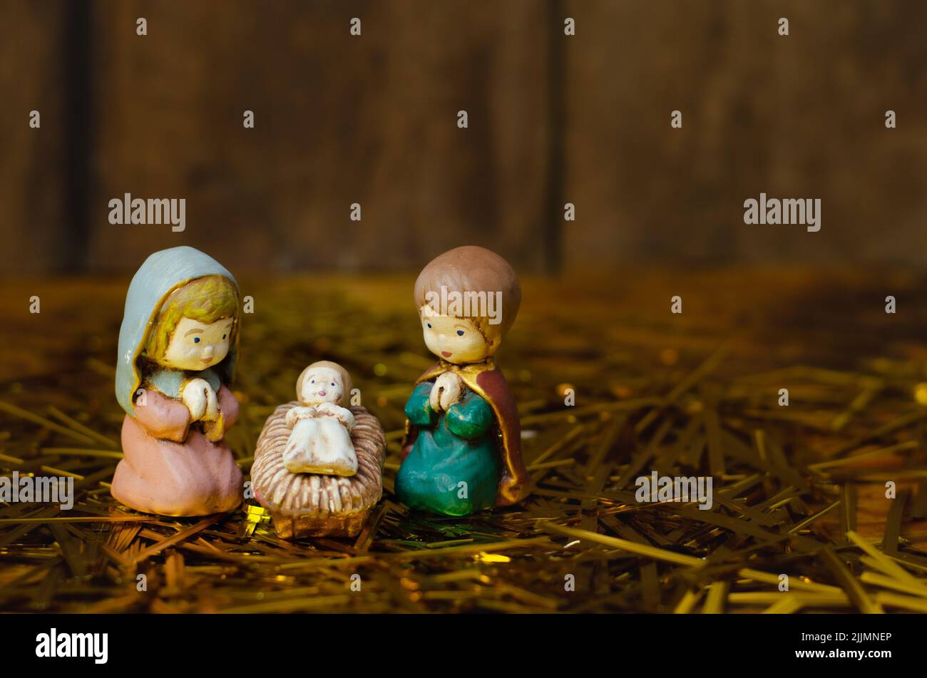 A close-up shot of mini colorful figures of the Nativity scene on hay ...