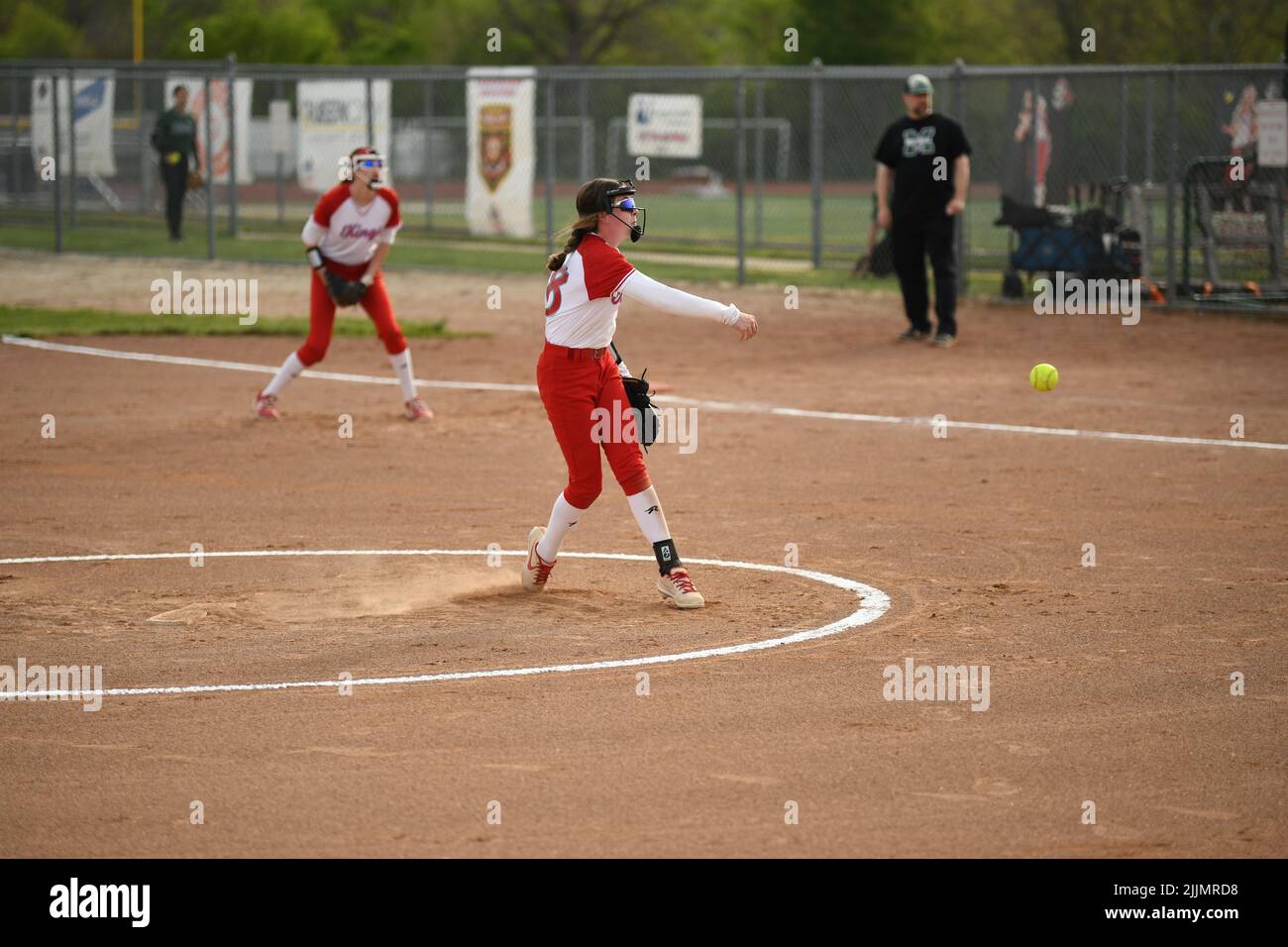 A girl in a red and white uniform playing softball with a team in the ...