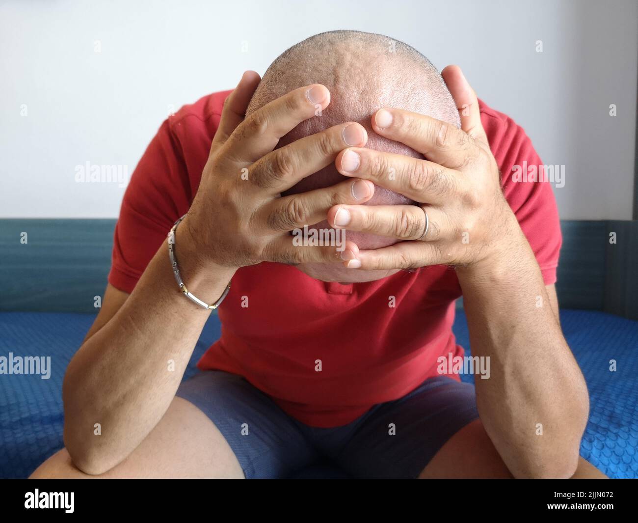 A close-up shot of a desperate bald man cries and putting his hands on ...