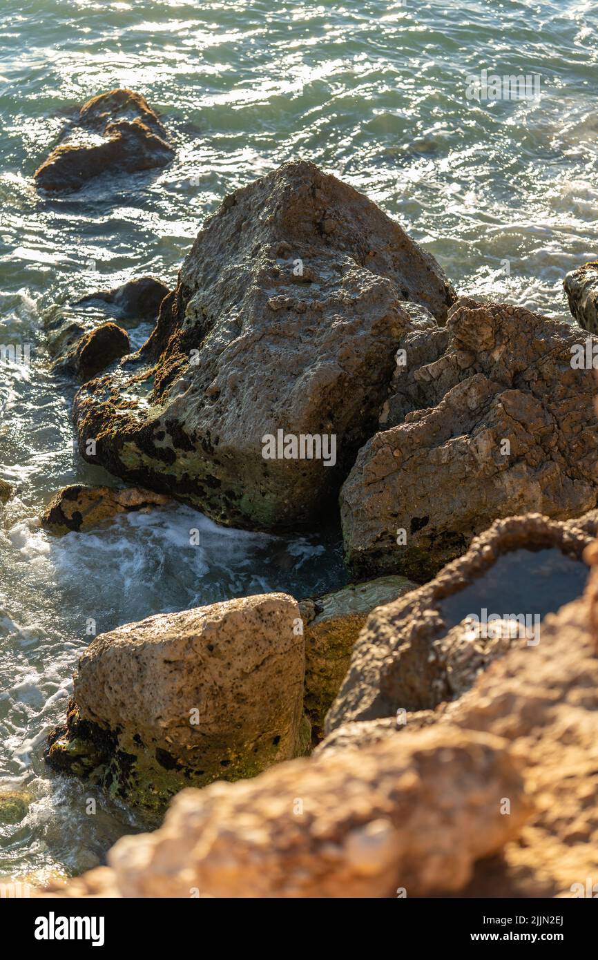A vertical shot of rocks on the beach shore with shiny water on a sunny ...