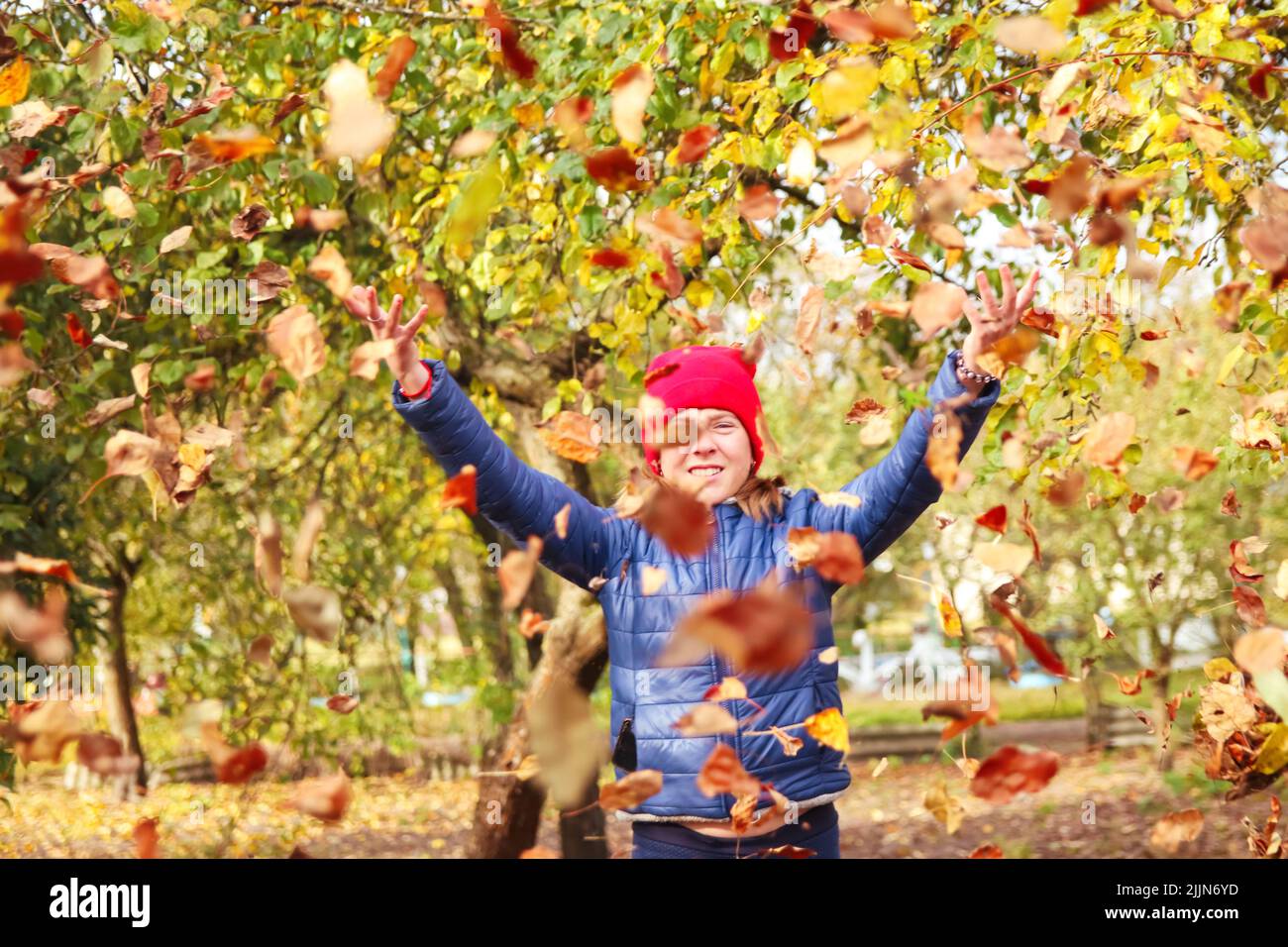 Defocus autumn people. Teen girl raising hand and throwing leaves. Many ...