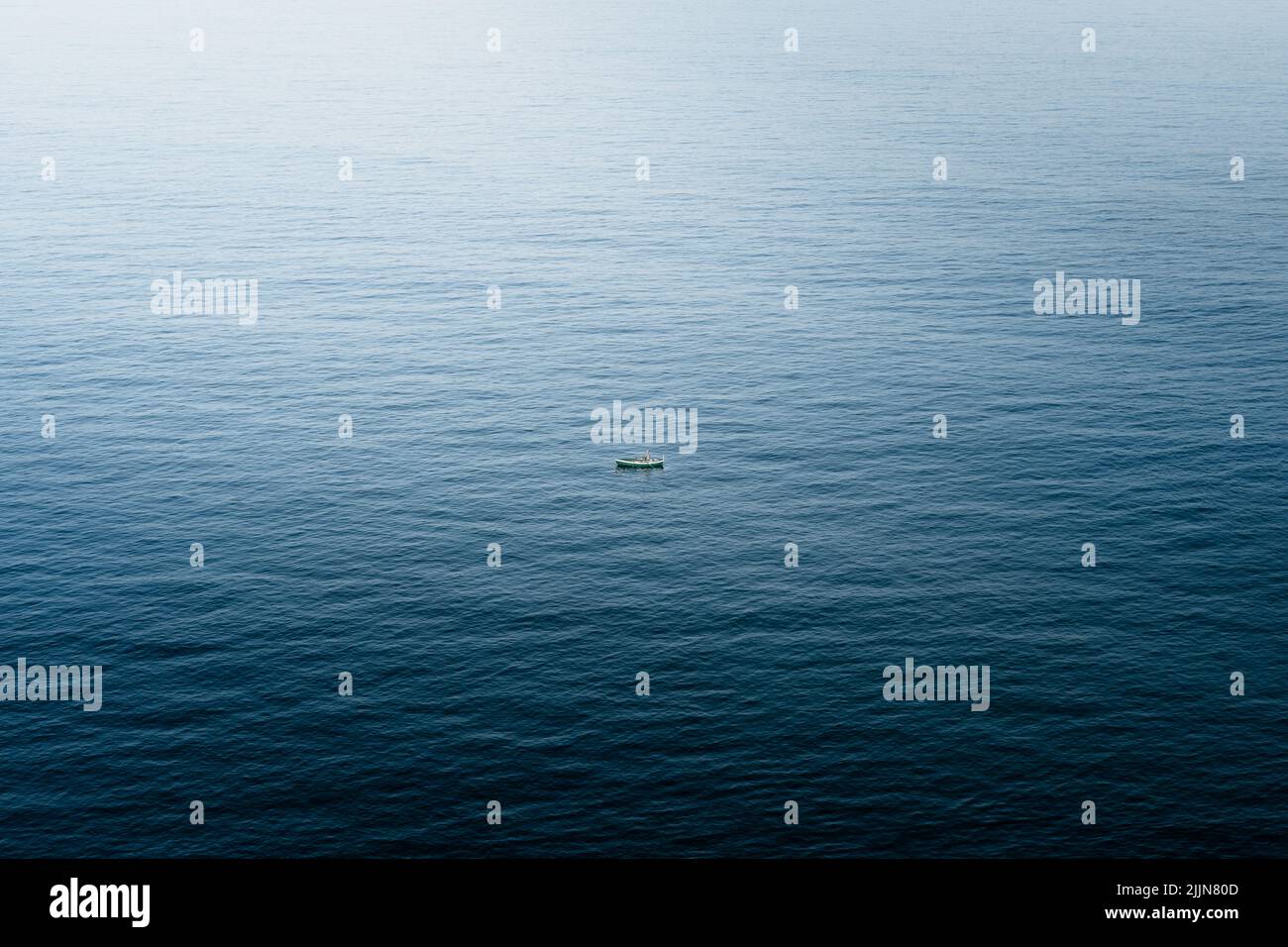 A scenic view of a body of water from afar with a small sailing boat in ...