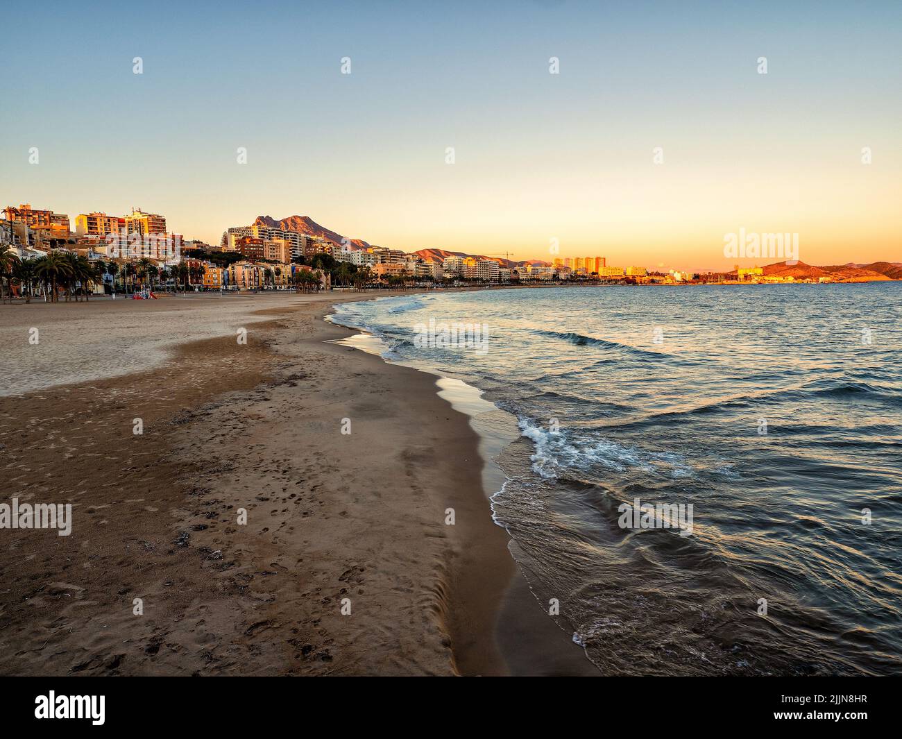 A calm beach along a coastal city under a clear sunset sky Stock Photo ...