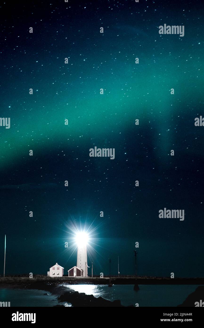 A vertical shot of Aurora borealis above a lighthouse in Reykjavik ...