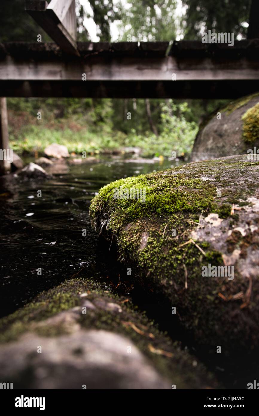 A vertical shot of rocks with moss under a bridge by the river Stock ...