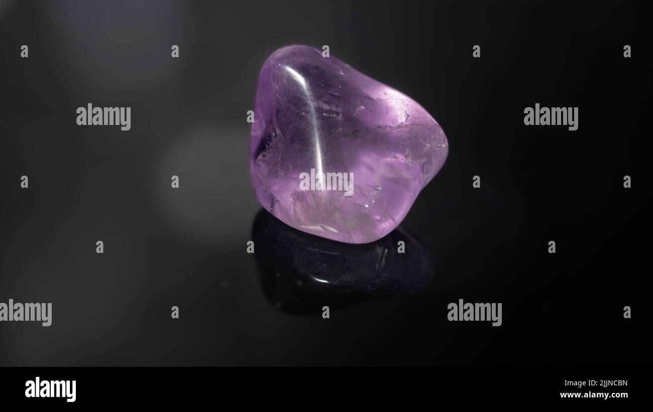 A polished pastel purple amethyst stone on a reflective black surface ...