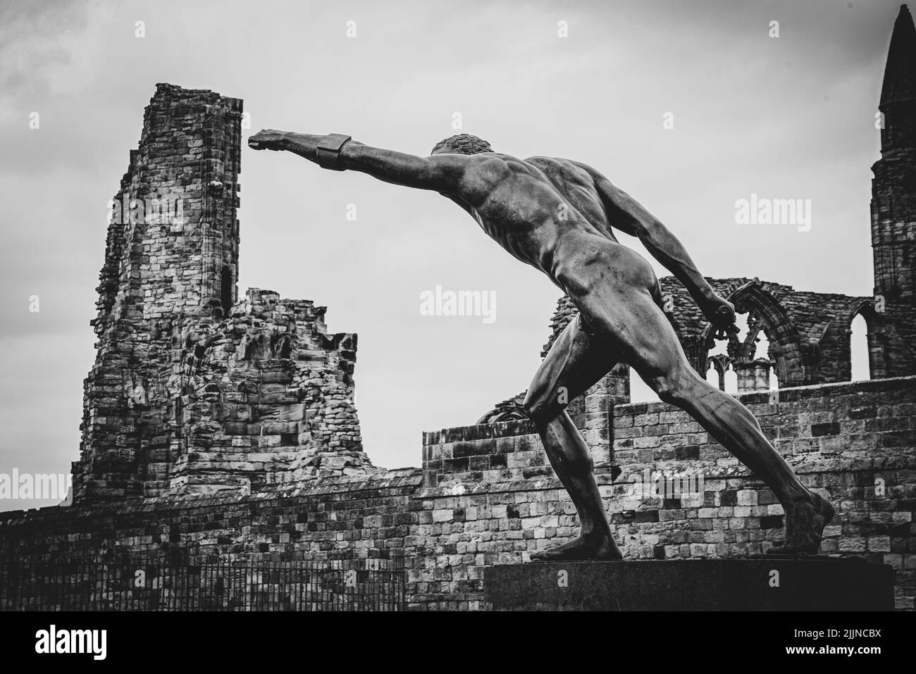 A grayscale shot of the Whitby Gladiator statue with the ruins of ...