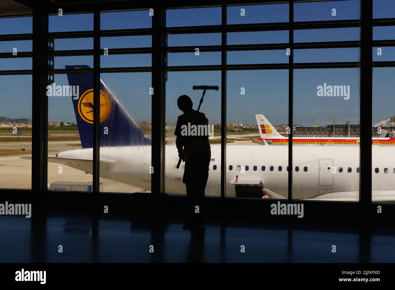 A person cleaning windows of an airport with a Lufthansa plane outside ...