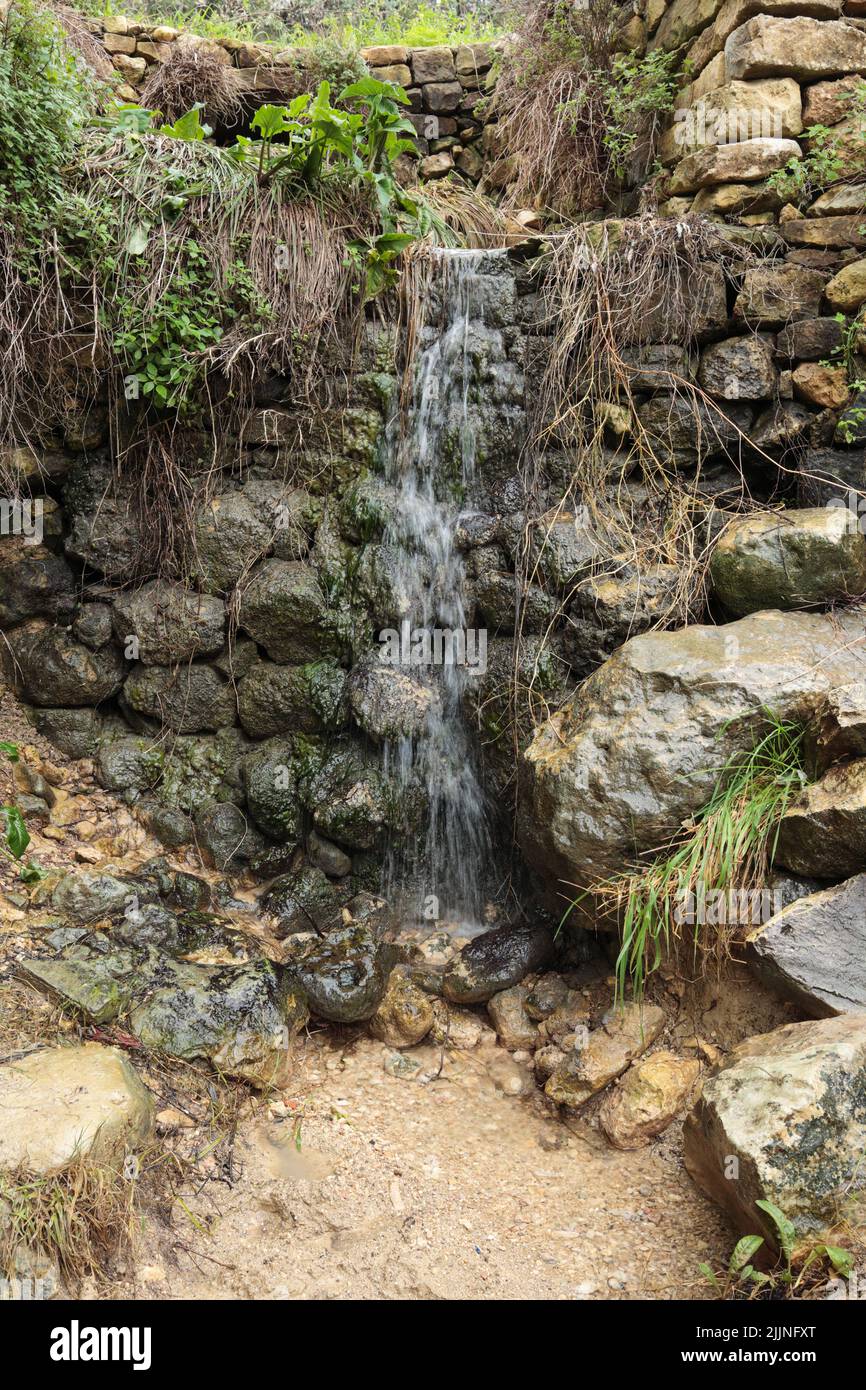 Stream tumbling over a rustic dry stone wall forming a small waterfall ...