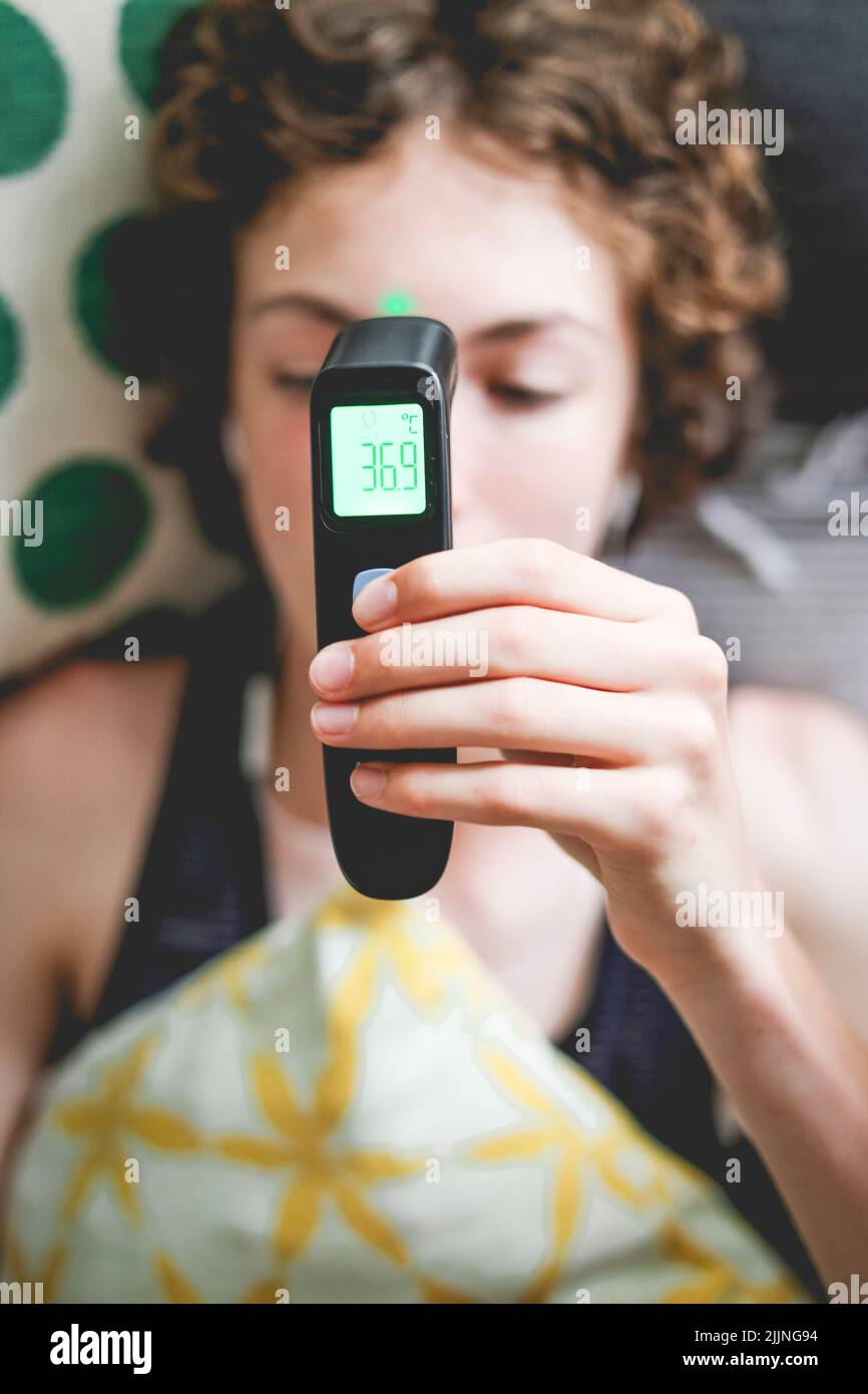 Teenager lying in bed taking his temperature with a digital thermometer ...