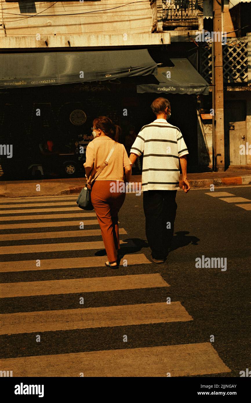 A vertical of an elderly couple holding hands while crossing the road ...
