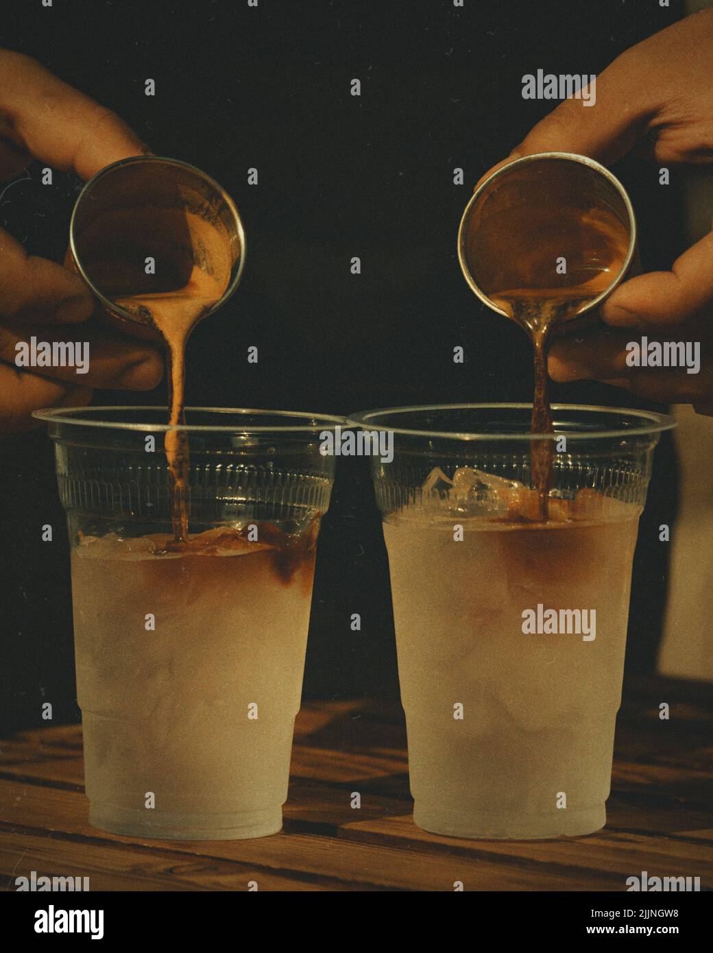 A vertical of a barista pouring coffee into the plastic cups filled ...