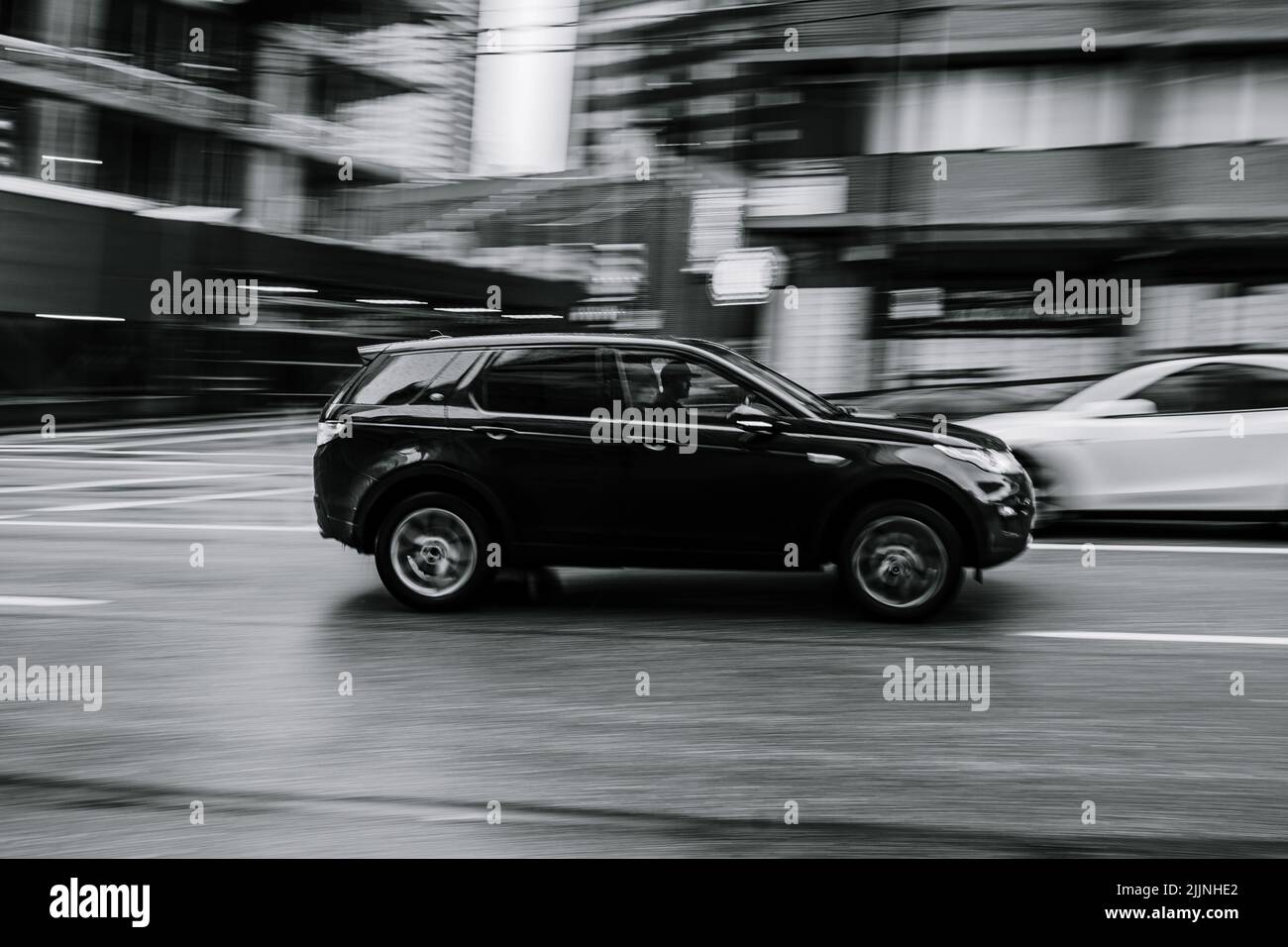 A grayscale of a range rover driving down a rainy street in Vancouver ...