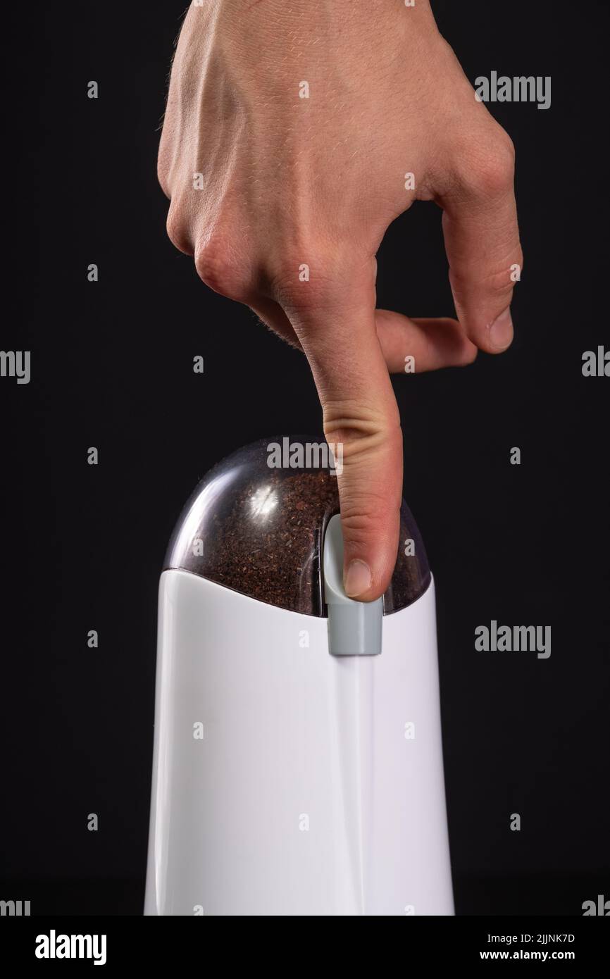 A vertical closeup of the hand pushing the button of the coffee grinder ...