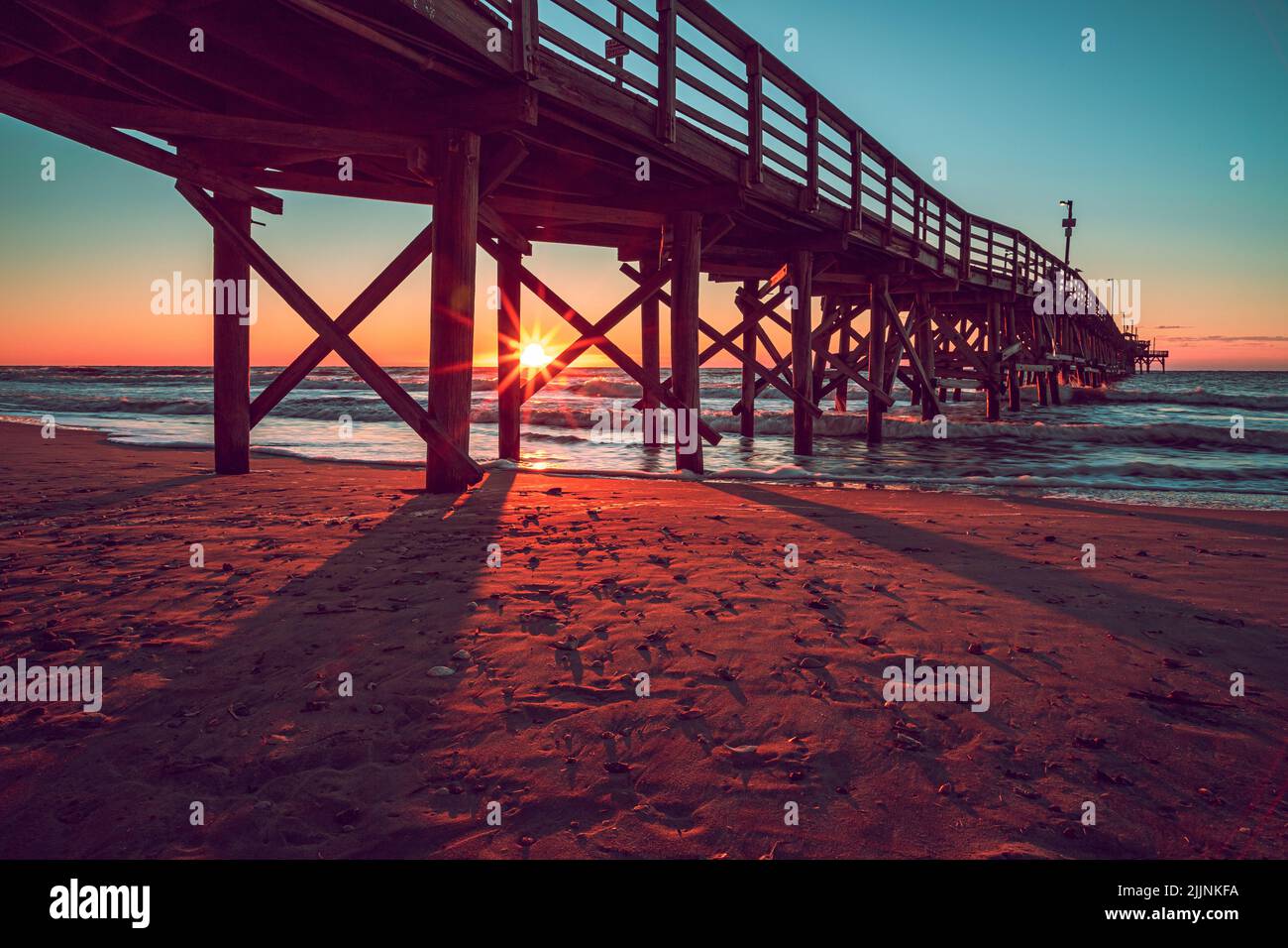 A beautiful view of the sunset at the beach over a big wooden bridge ...
