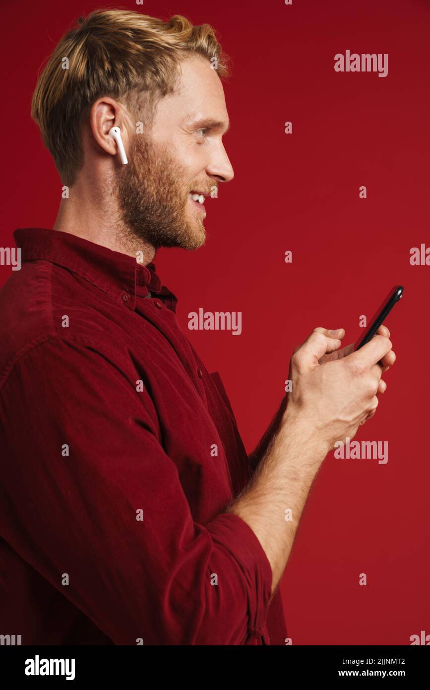 Blonde man listening music with earphones and using cellphone isolated ...