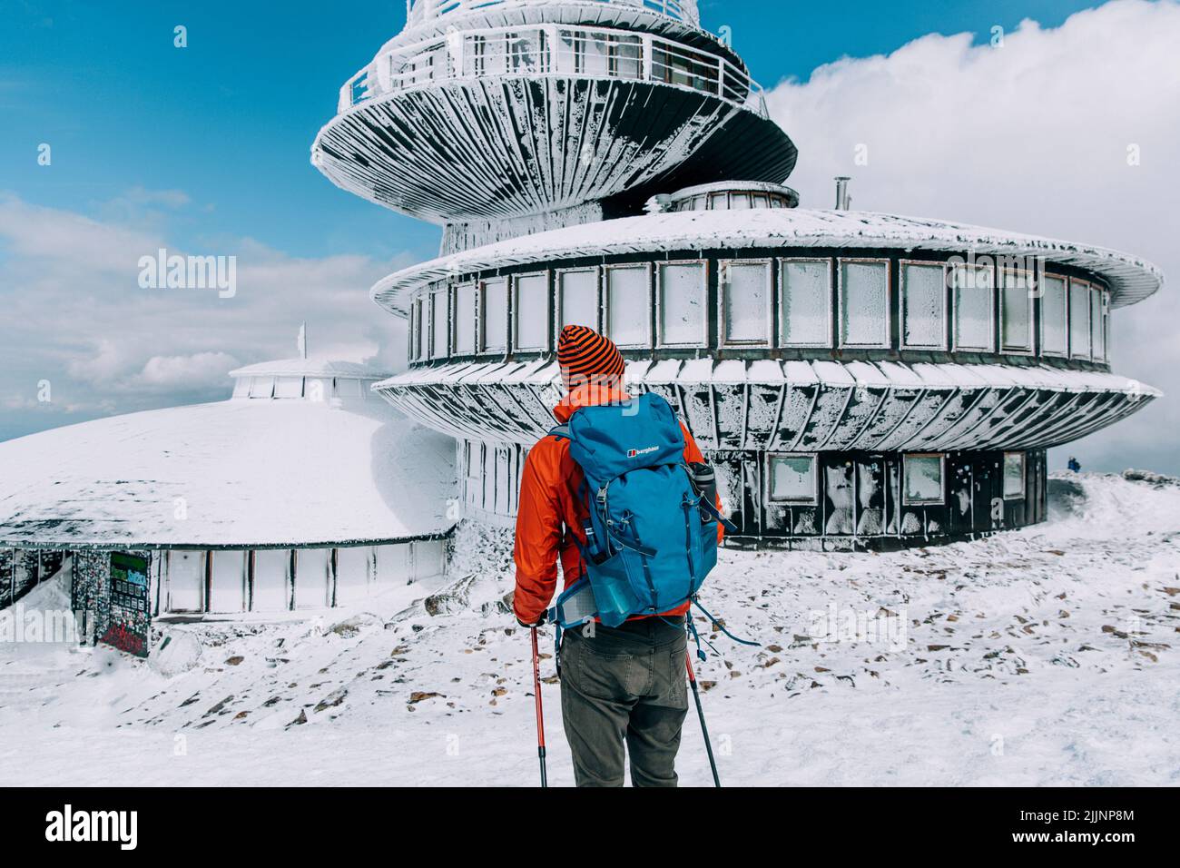 A back view of a hiker on a snowy mountain near a weather station in ...