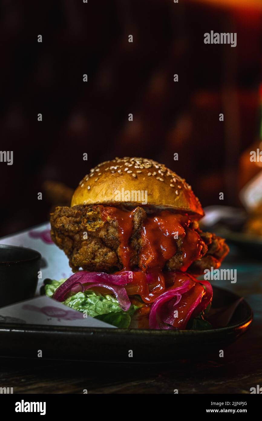 A vertical shot of a chicken burger in a dark grungy restaurant setting ...