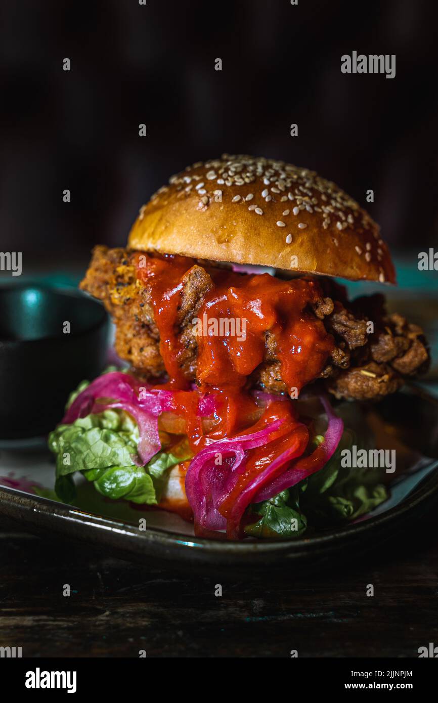A vertical shot of a chicken burger in a dark grungy restaurant setting ...