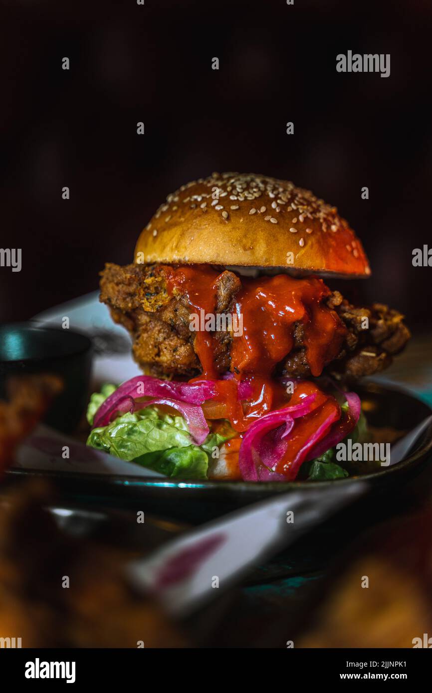 A vertical shot of a chicken burger in a dark grungy restaurant setting ...