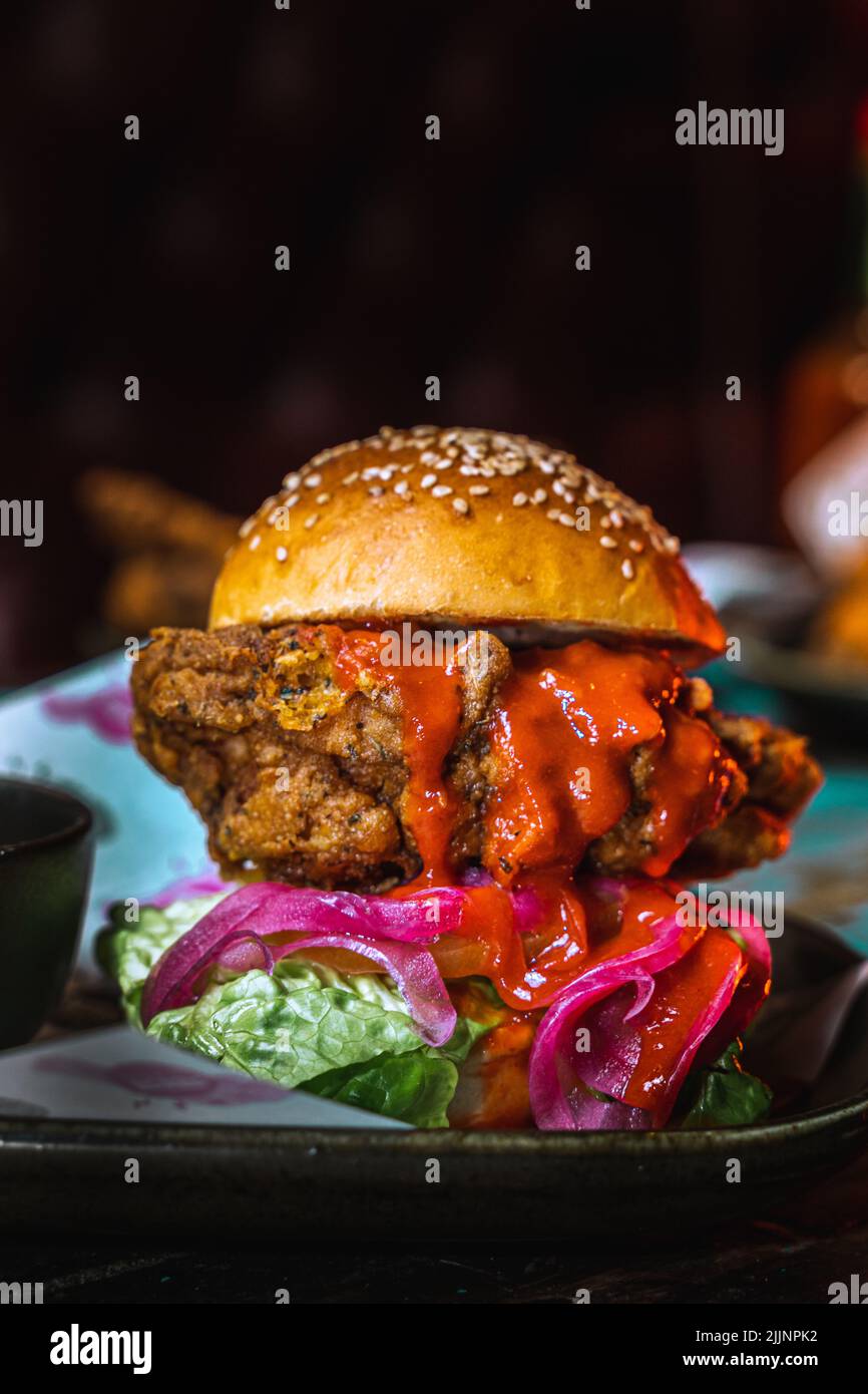 A vertical shot of a chicken burger in a dark grungy restaurant setting ...