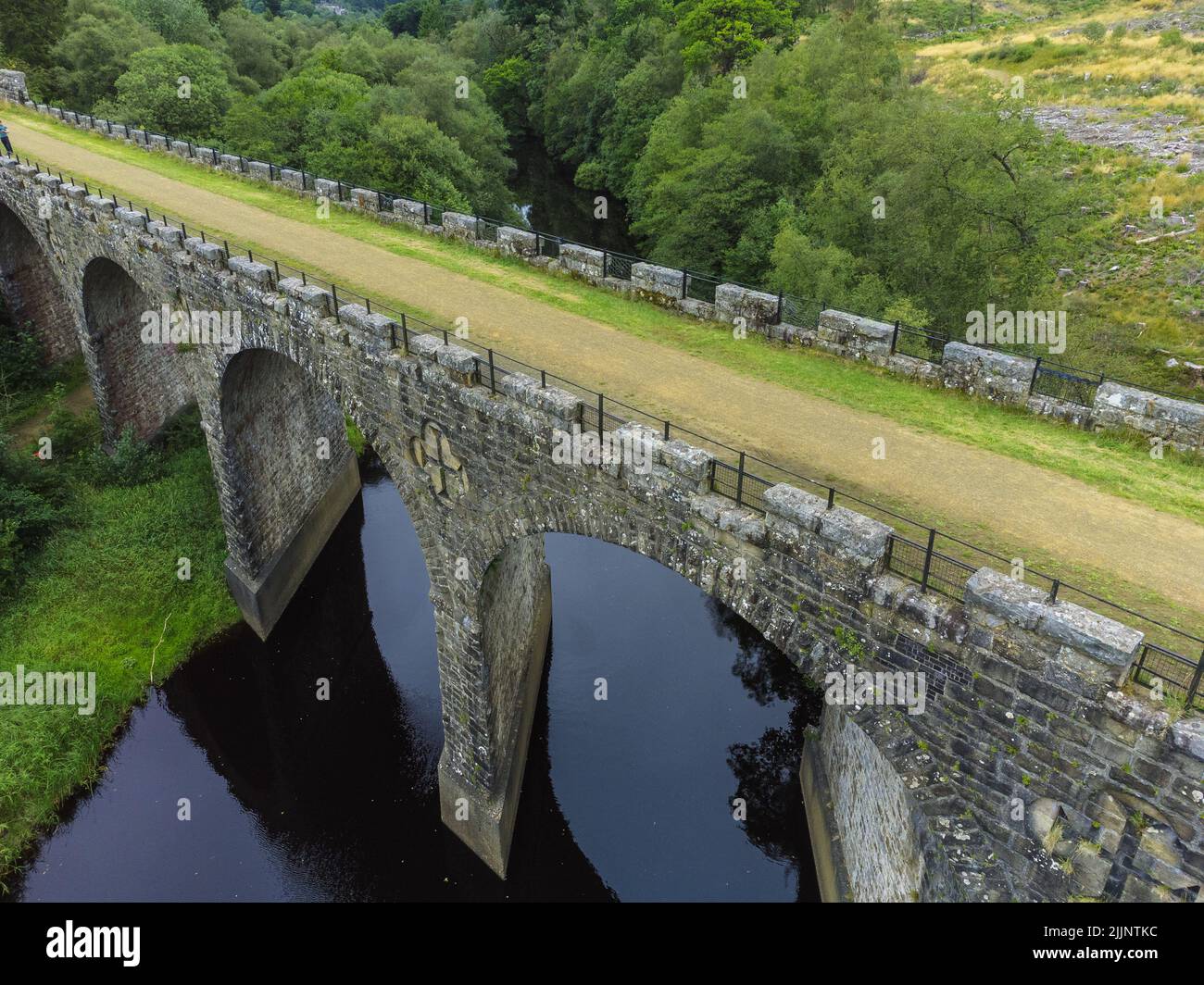An old stone bridge over the reflective river with dense green ...
