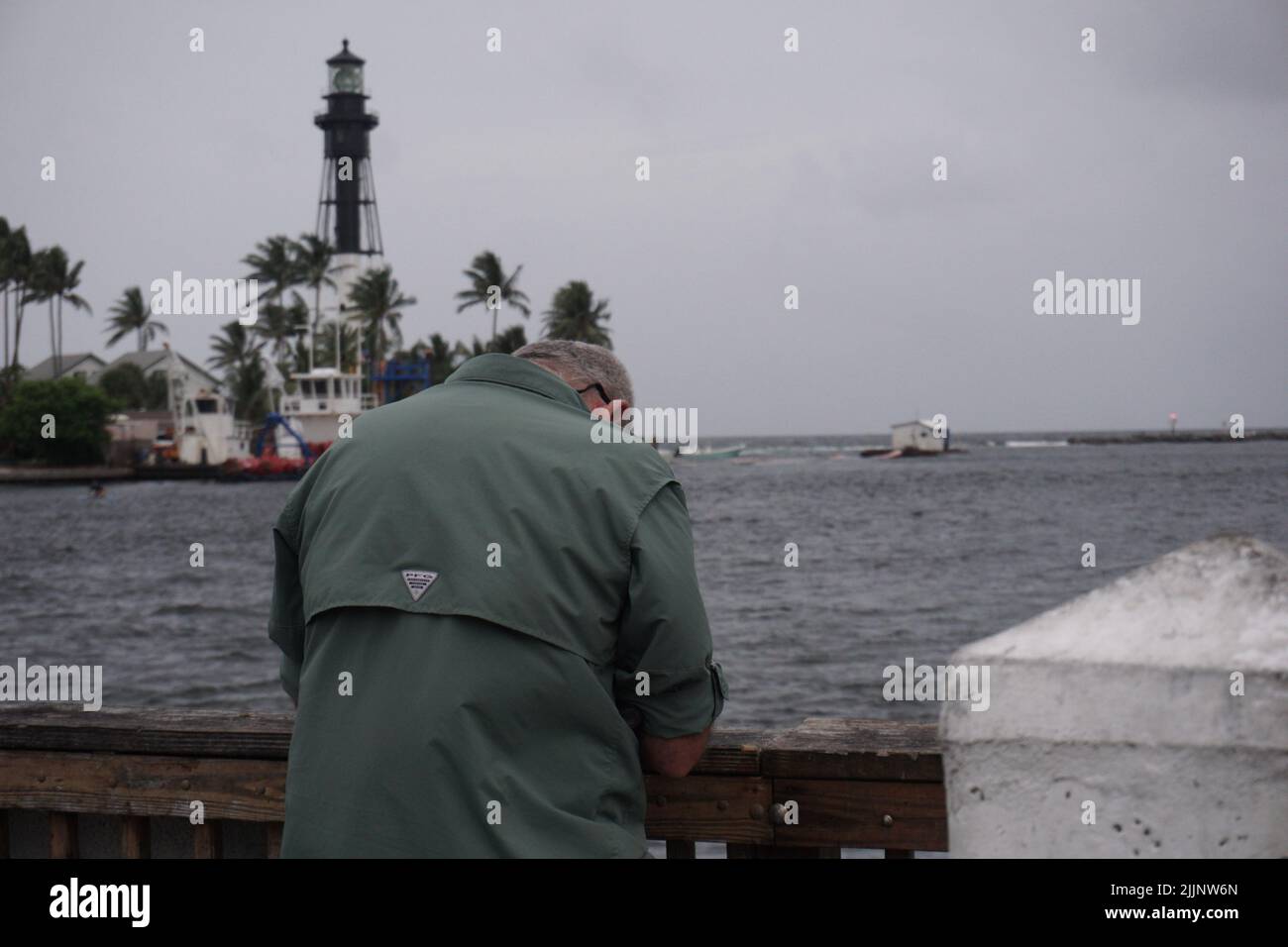A closeup of a man leaning against a wooden barricade at the beach on a ...