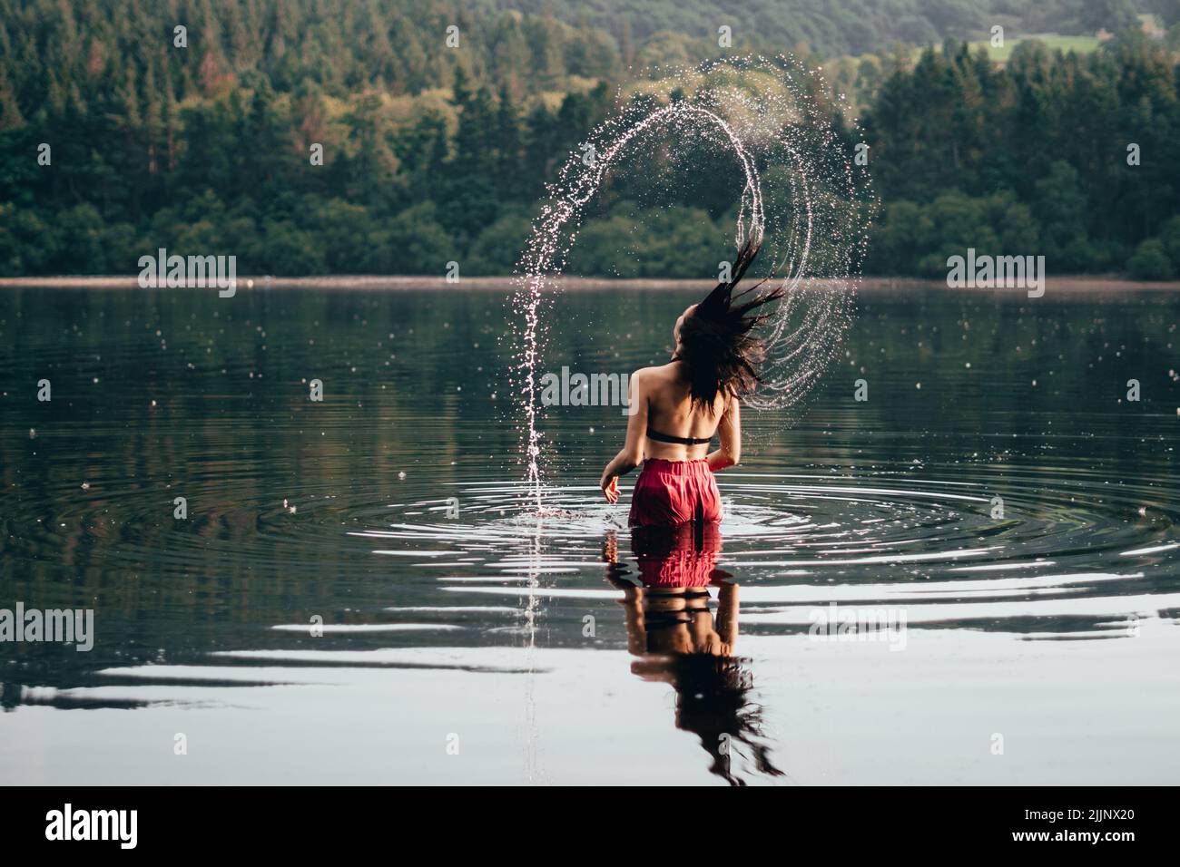 A back view of female throwing her wet hair back and splashing water in ...
